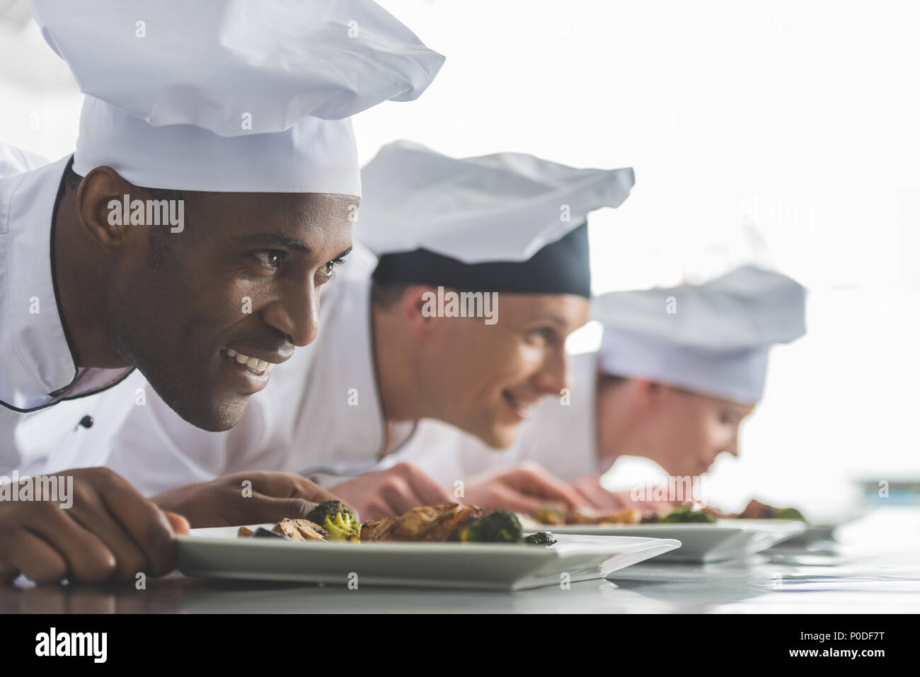 smiling multicultural chefs sniffing cooked food at restaurant kitchen ...