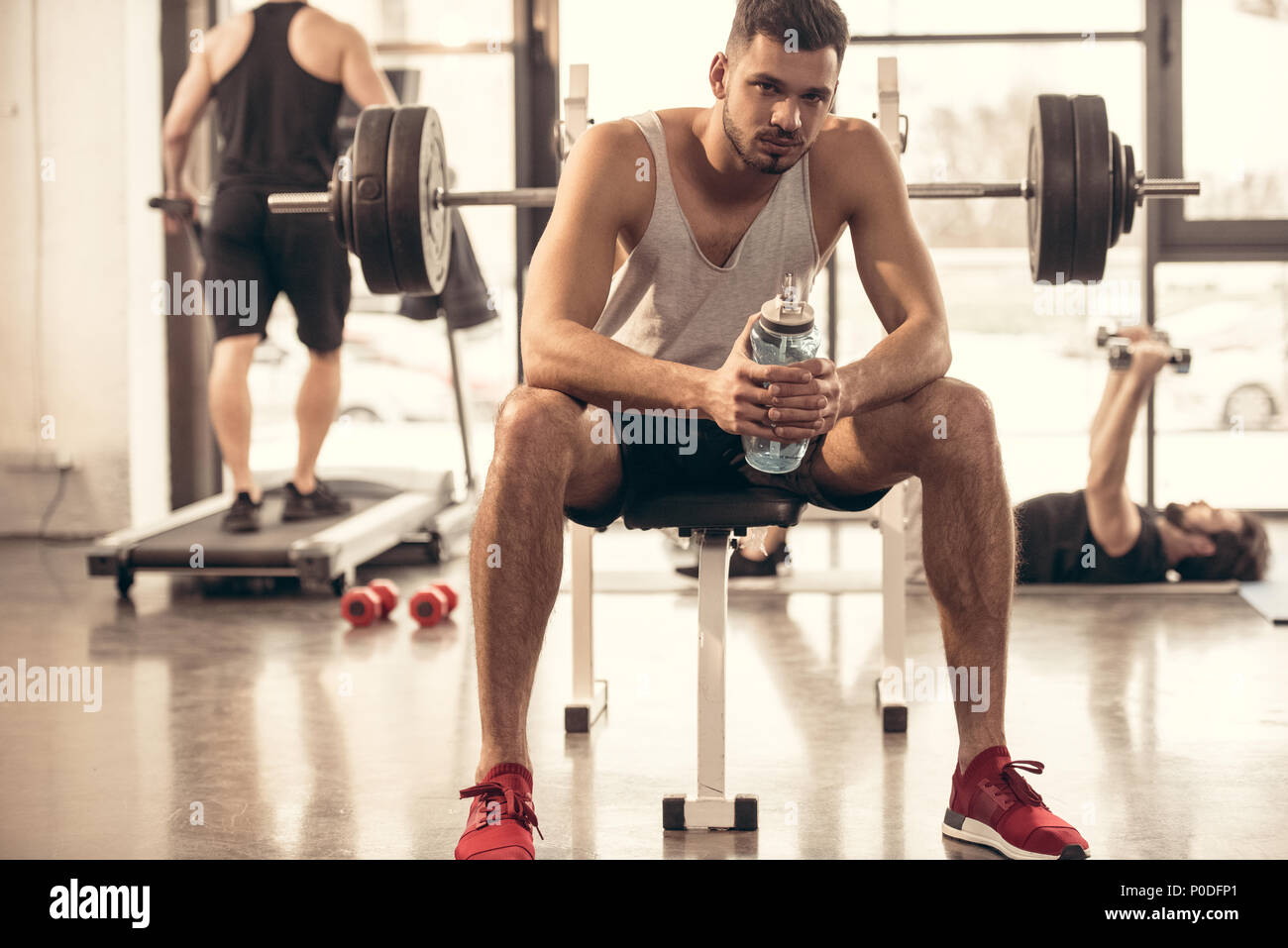 handsome sportsman sitting with bottle of water on bench press in gym ...