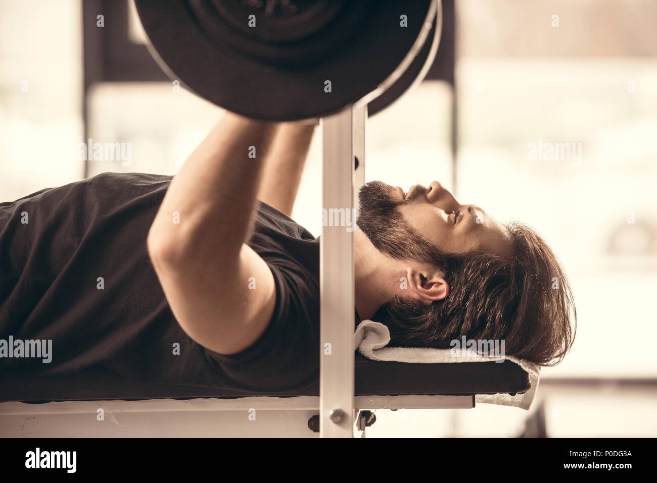 side view of handsome sportsman lifting barbell with weight plates in ...