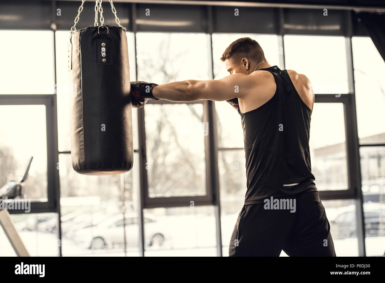 side view of muscular young boxer training with punching bag in gym ...