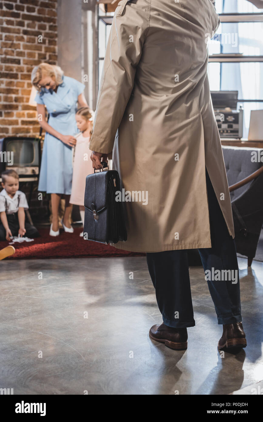 cropped shot of father with briefcase coming home while happy family ...