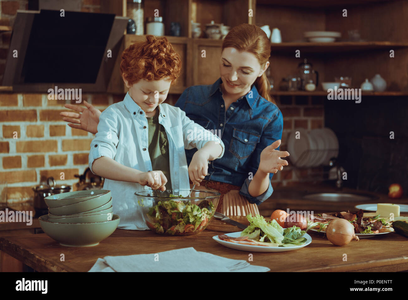 portrait of little son helping mother cooking dinner in kitchen at home ...