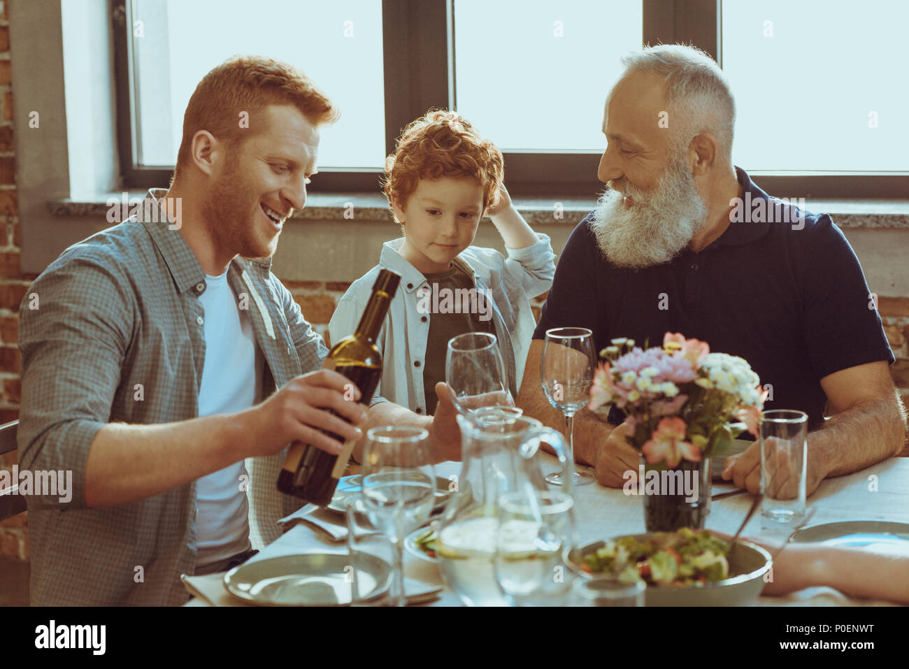smiling men having dinner at home while grandson standing at table ...