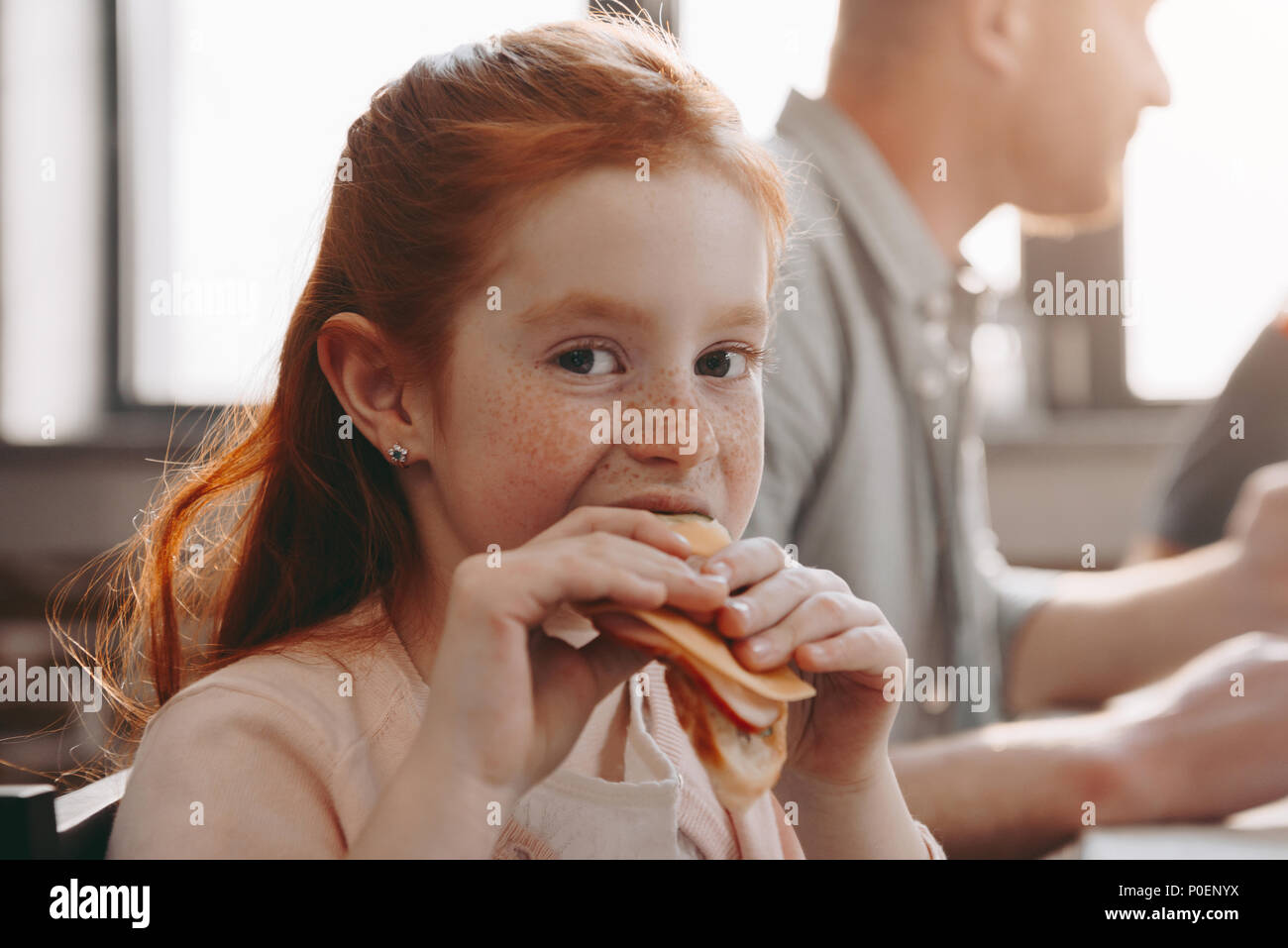 selective focus of little girl looking at camera while eating sandwich ...