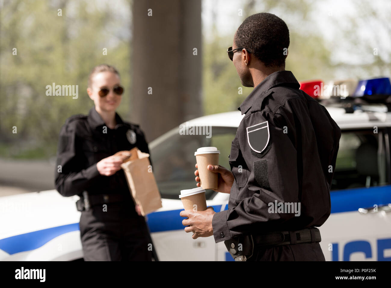 young police officers with coffee to go and paper bag with lunch having ...