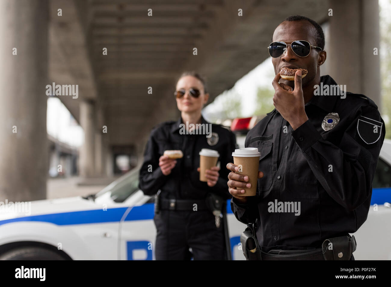 young police officers having coffee break with doughnuts in front of ...