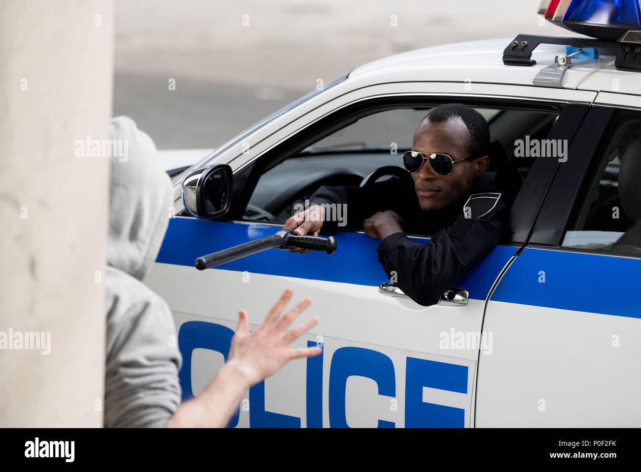 african american policeman stopping hooded man with police bat while ...