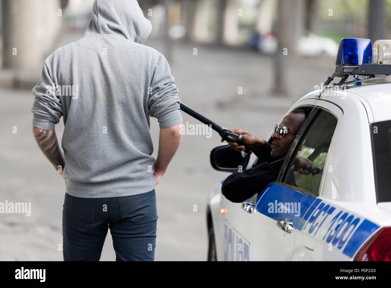rear view of african american policeman stopping hooded man with police ...