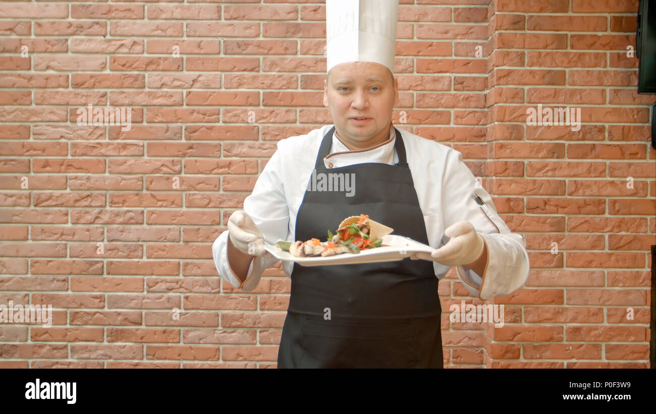 Friendly chef in uniform present a plate with seafood salad, talking to ...