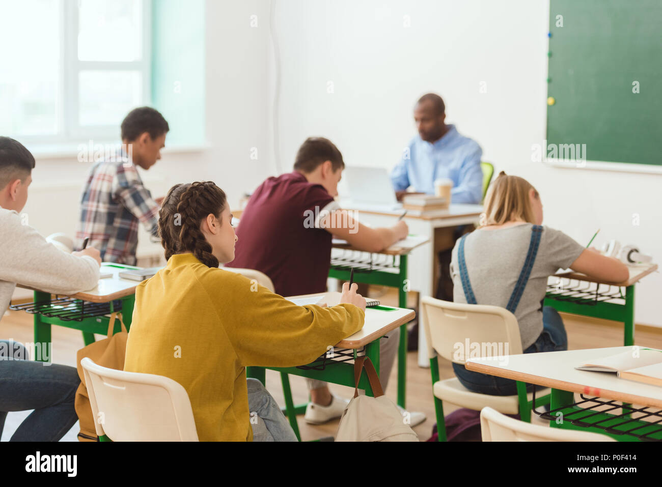 Rear view of high school pupils writing and african american typing on ...