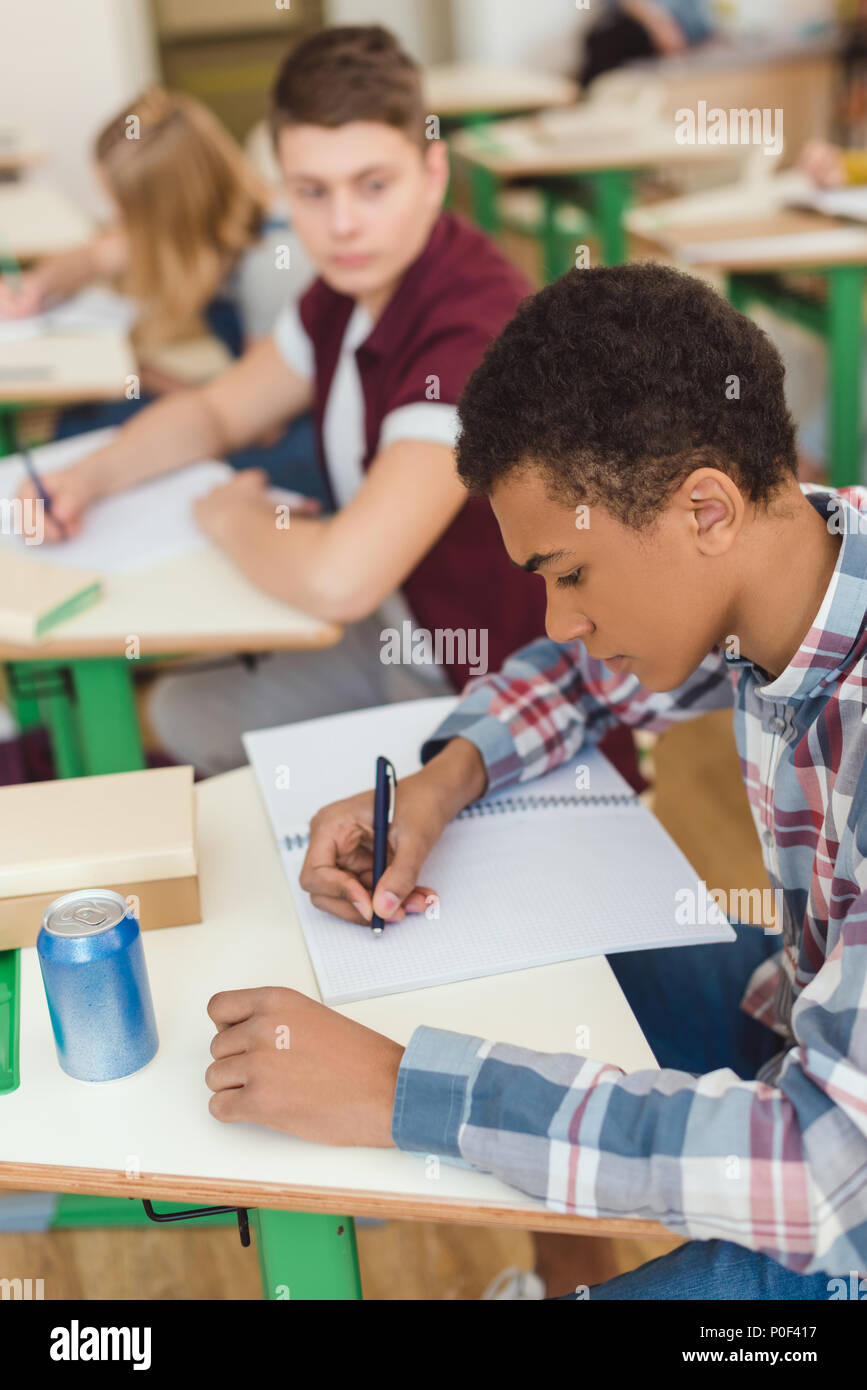 Elevated view of african american teenage schoolboy writing in textbook ...