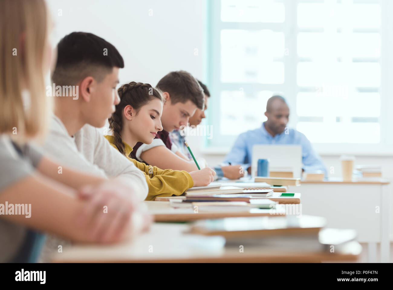Side view of schoolchildren sitting in row and teacher at table with ...