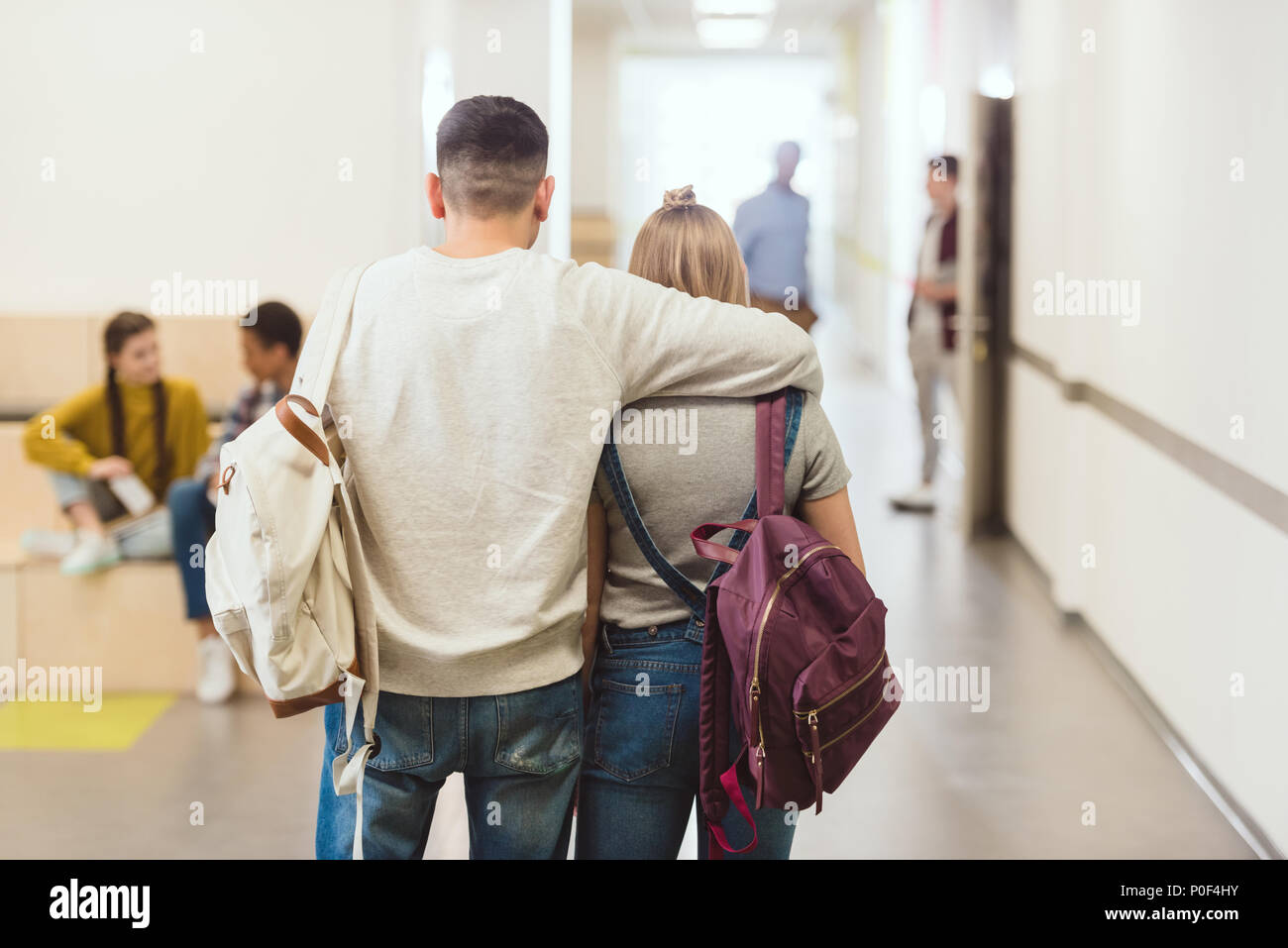 back view of teenage students couple walking by school corridor and ...