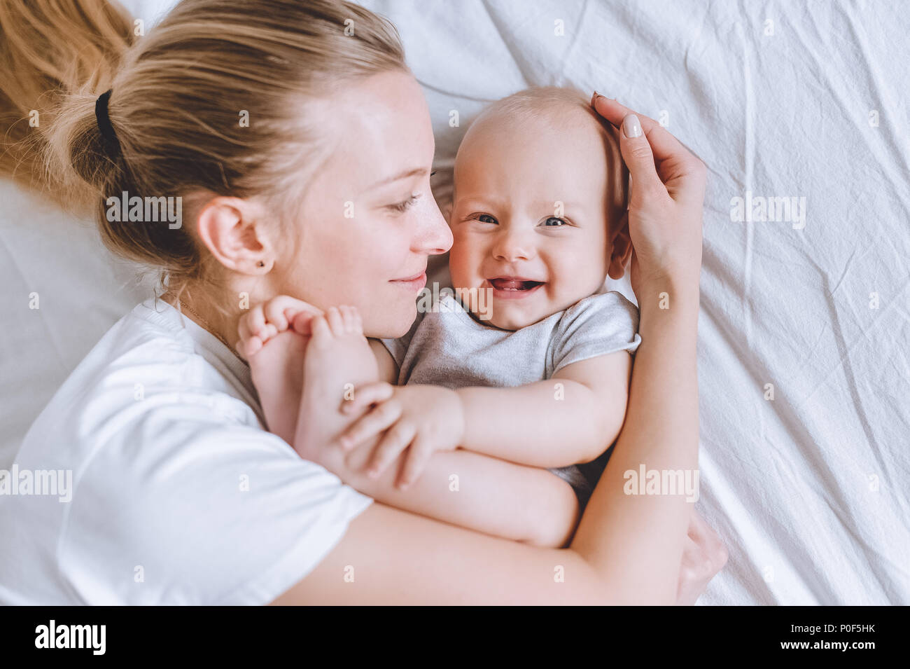 top view of mother cuddling her laughing infant baby in bed Stock Photo ...