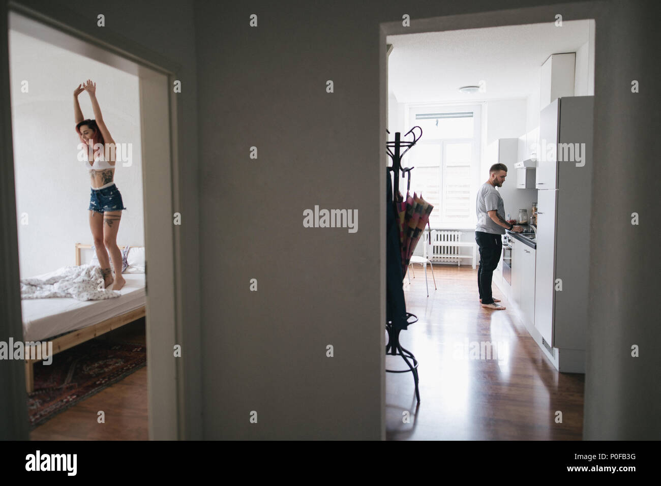 man cooking in kitchen while happy girlfriend jumping on bed in bedroom ...