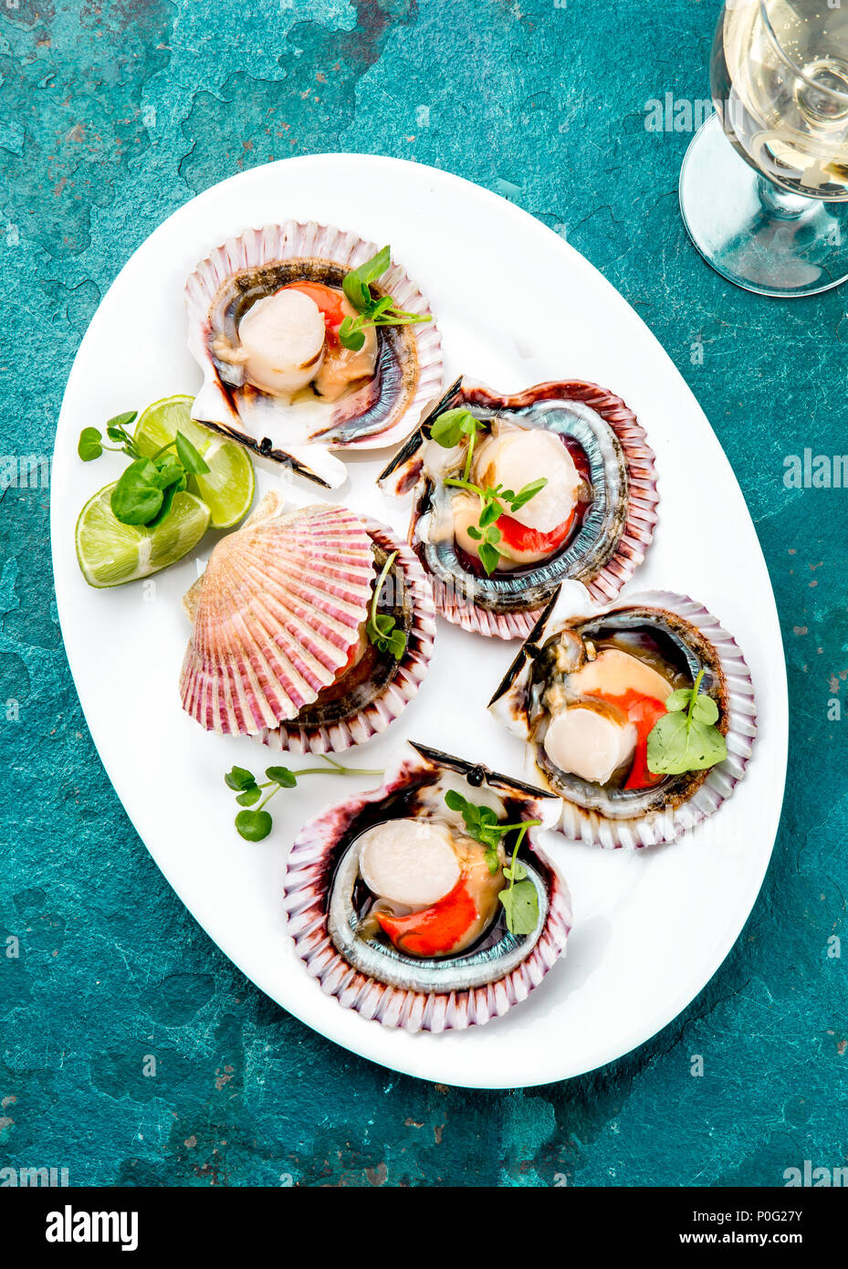 Raw opened shellfish scallops on white plate served with lemon and ...