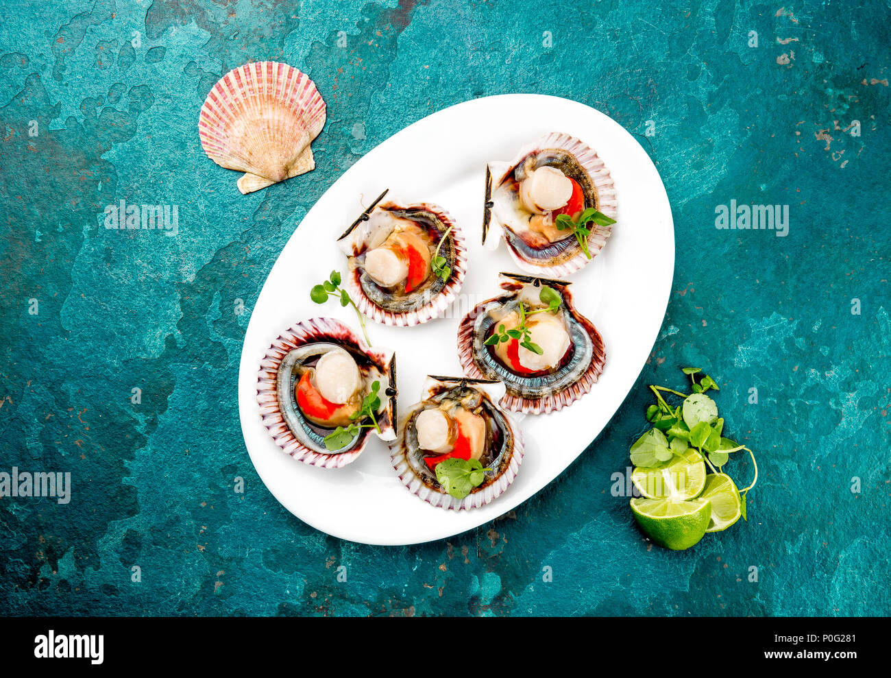 Raw opened shellfish scallops on white plate served with lemon and ...