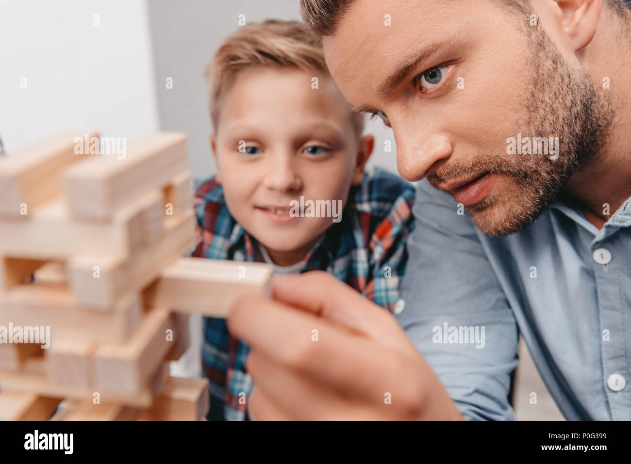 Father pulling a piece out of blocks wood tower while son is watching ...