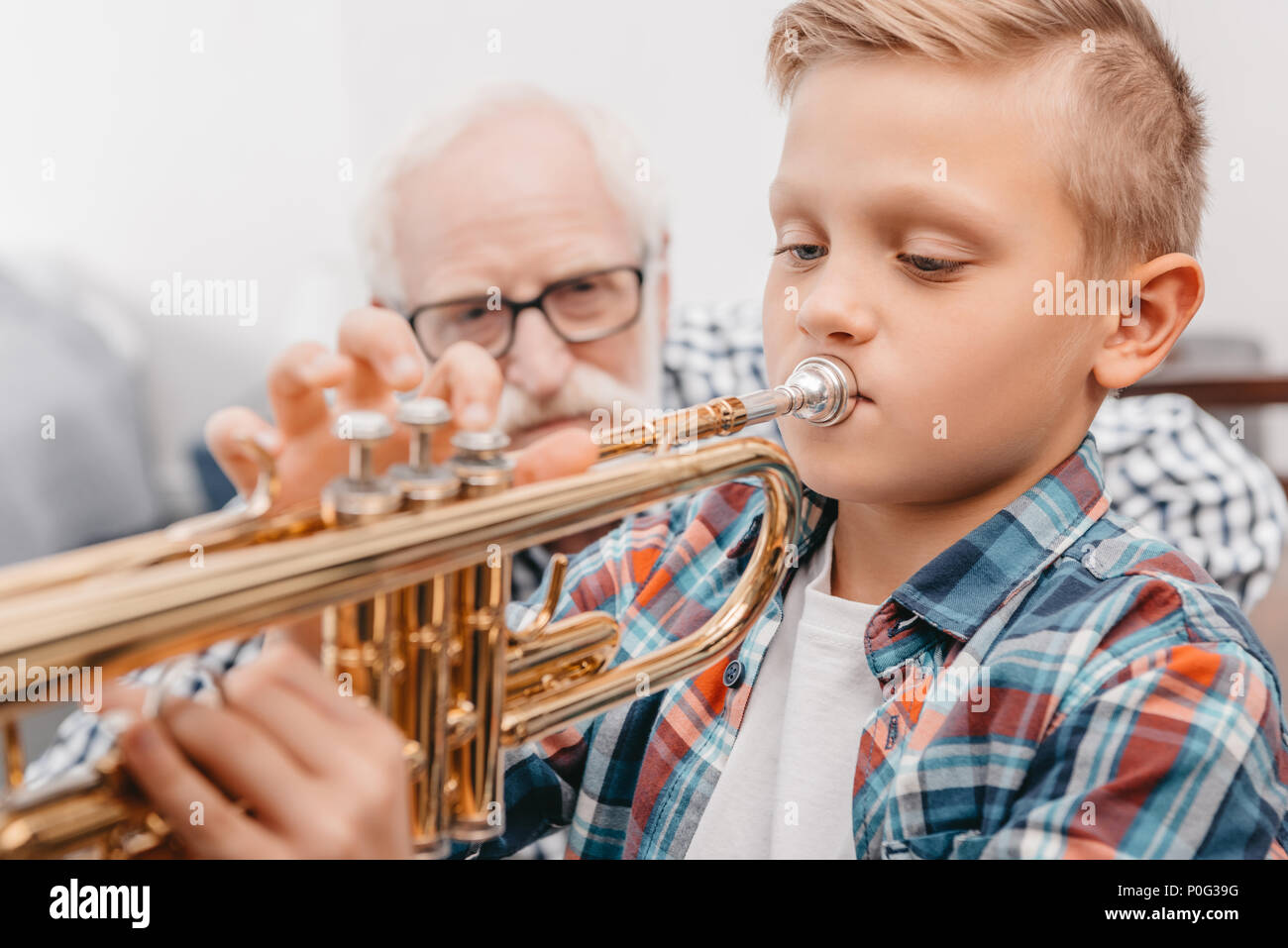 Little boy practicing playing trumpet while his grandfather is watching ...