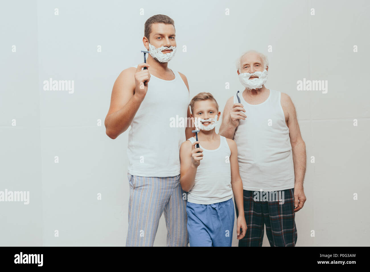 Father, son and grandfather standing with shaving cream on their faces ...