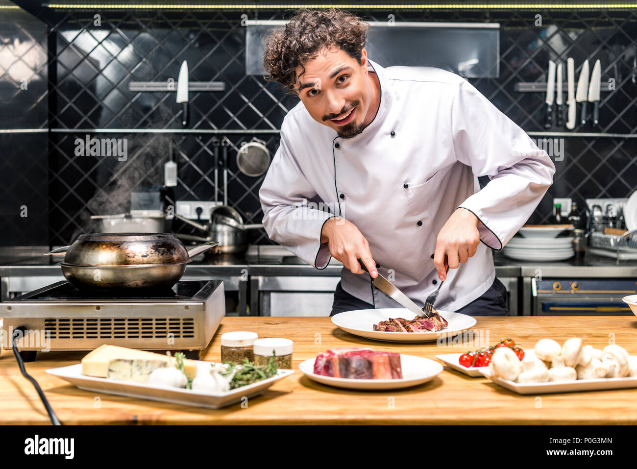 smiling chef cutting fried meat with knife and fork Stock Photo - Alamy