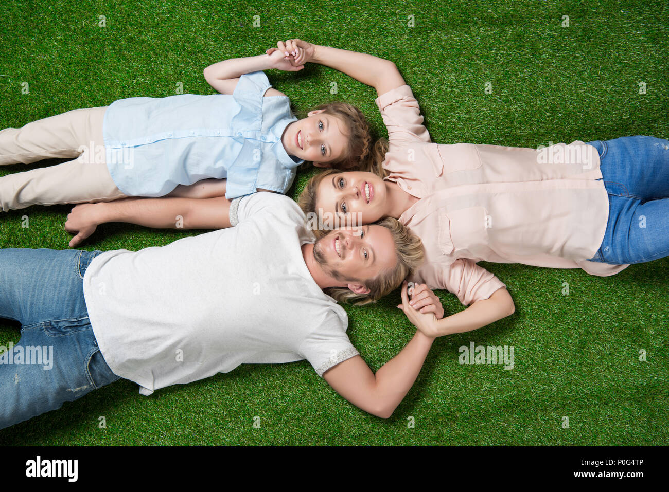 above view of happy family looking at camera while lying on the grass ...