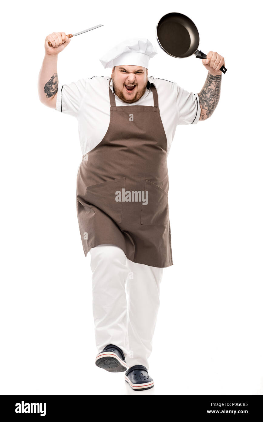 angry chef with frying pan and knife in hands looking at camera ...