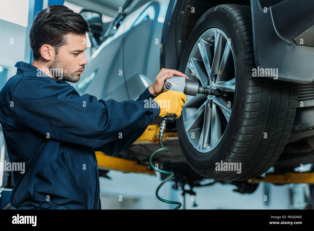 Automechanic unscrewing tire bolts on a lifted up car at a repair shop ...