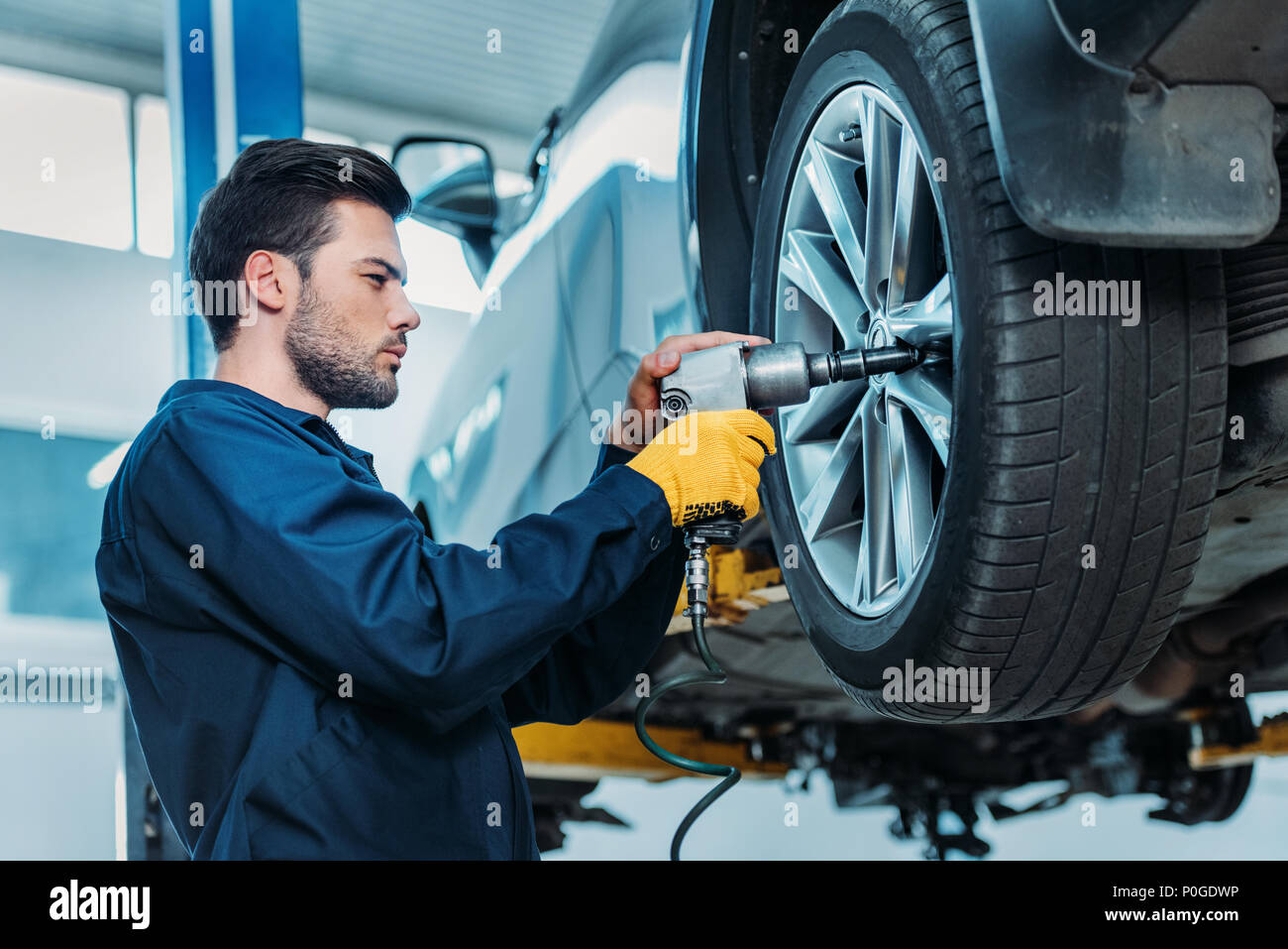 Automechanic unscrewing tire bolts on a lifted up car at a repair shop ...