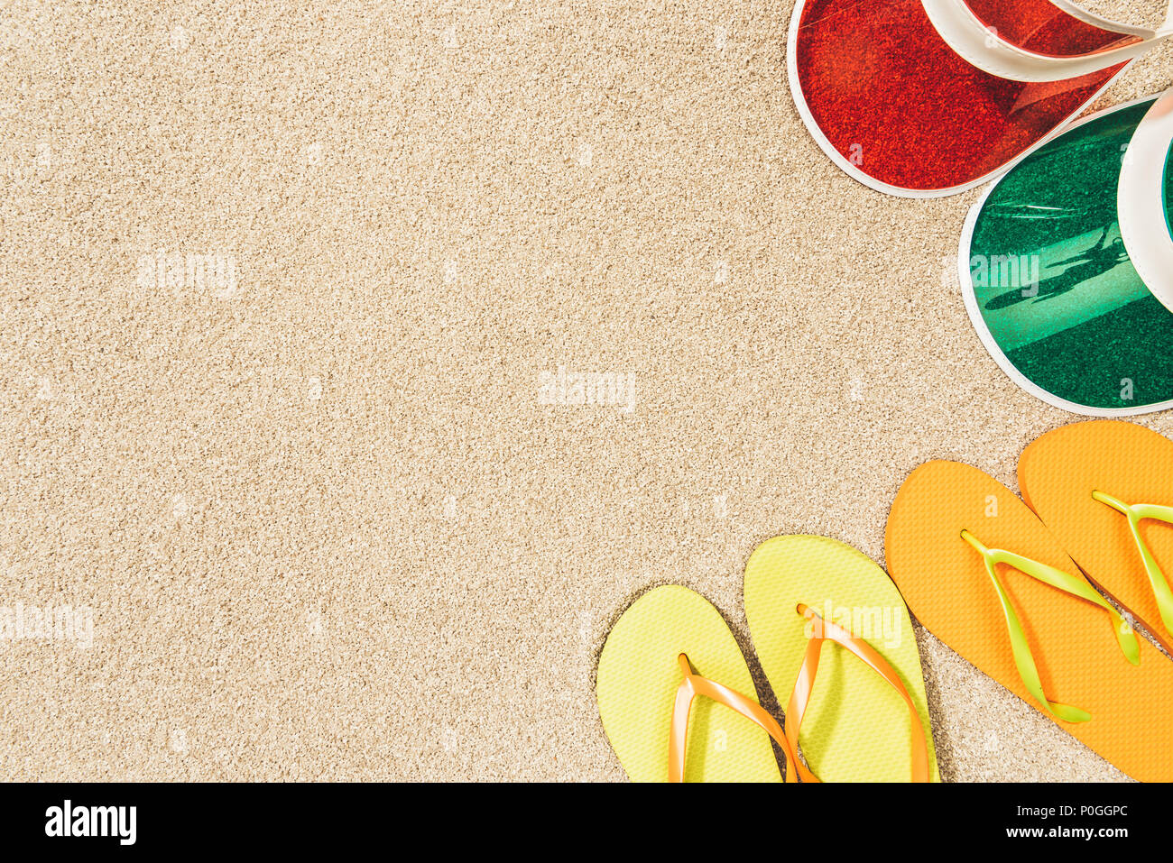 flat lay with colorful flip flops and caps arranged on sand Stock Photo ...