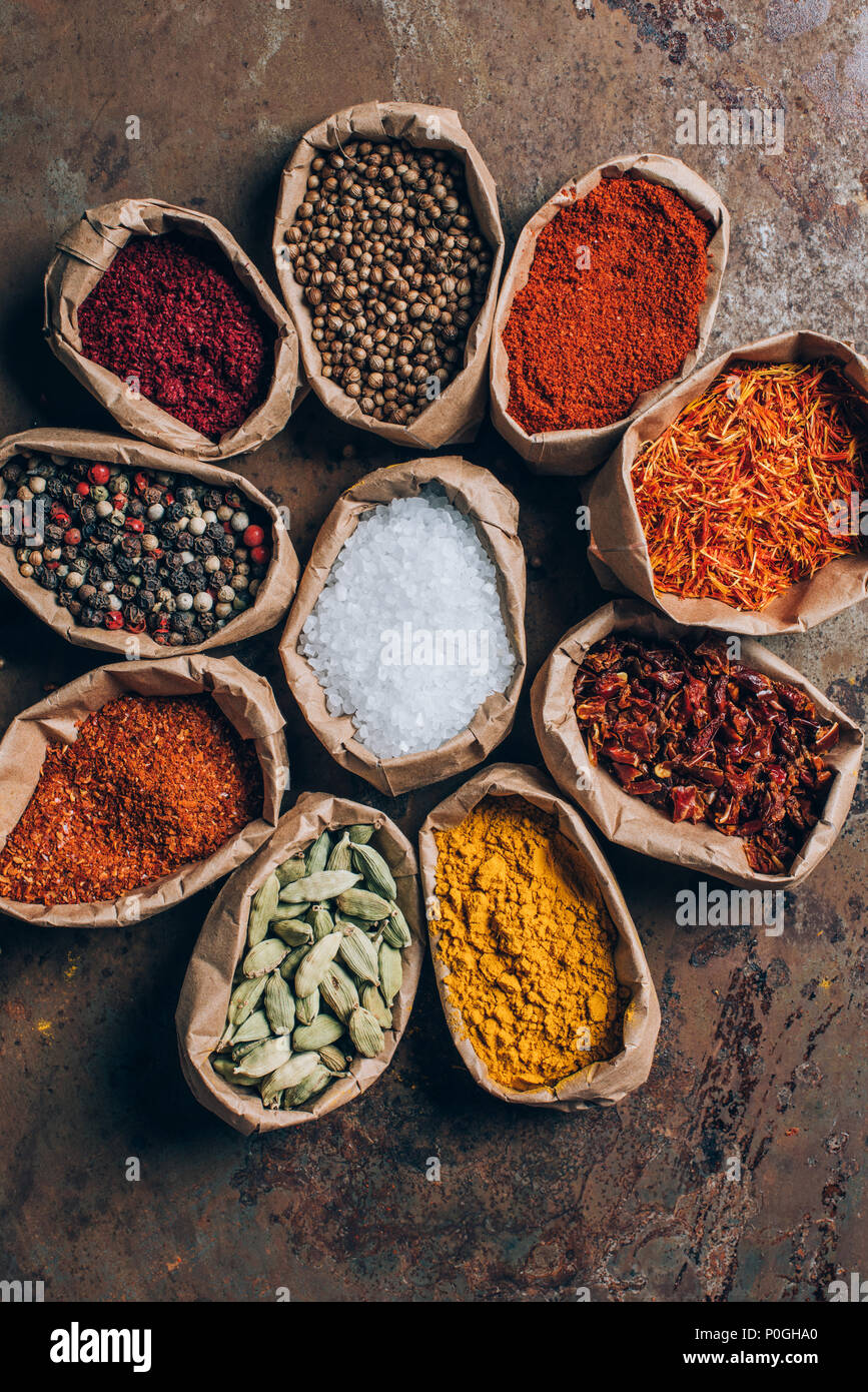 top view of coriander, saffron and chilli flakes in paper bags on table ...