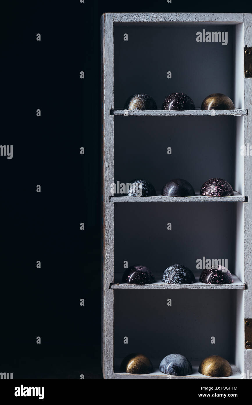 various chocolate candies placed in rows on shelves on black background ...