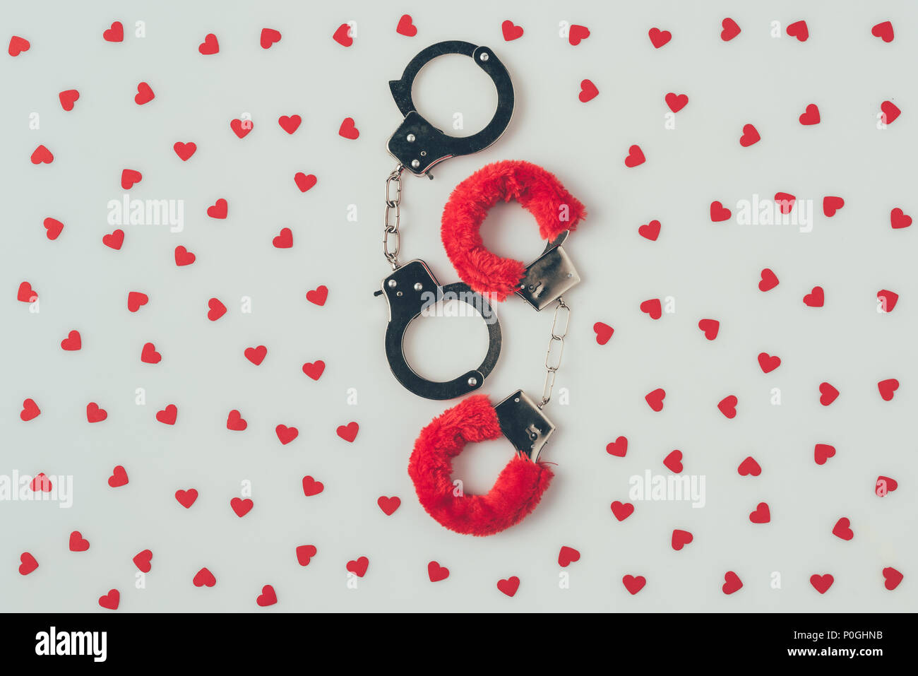 top view of black and red handcuffs with scattered paper hearts ...