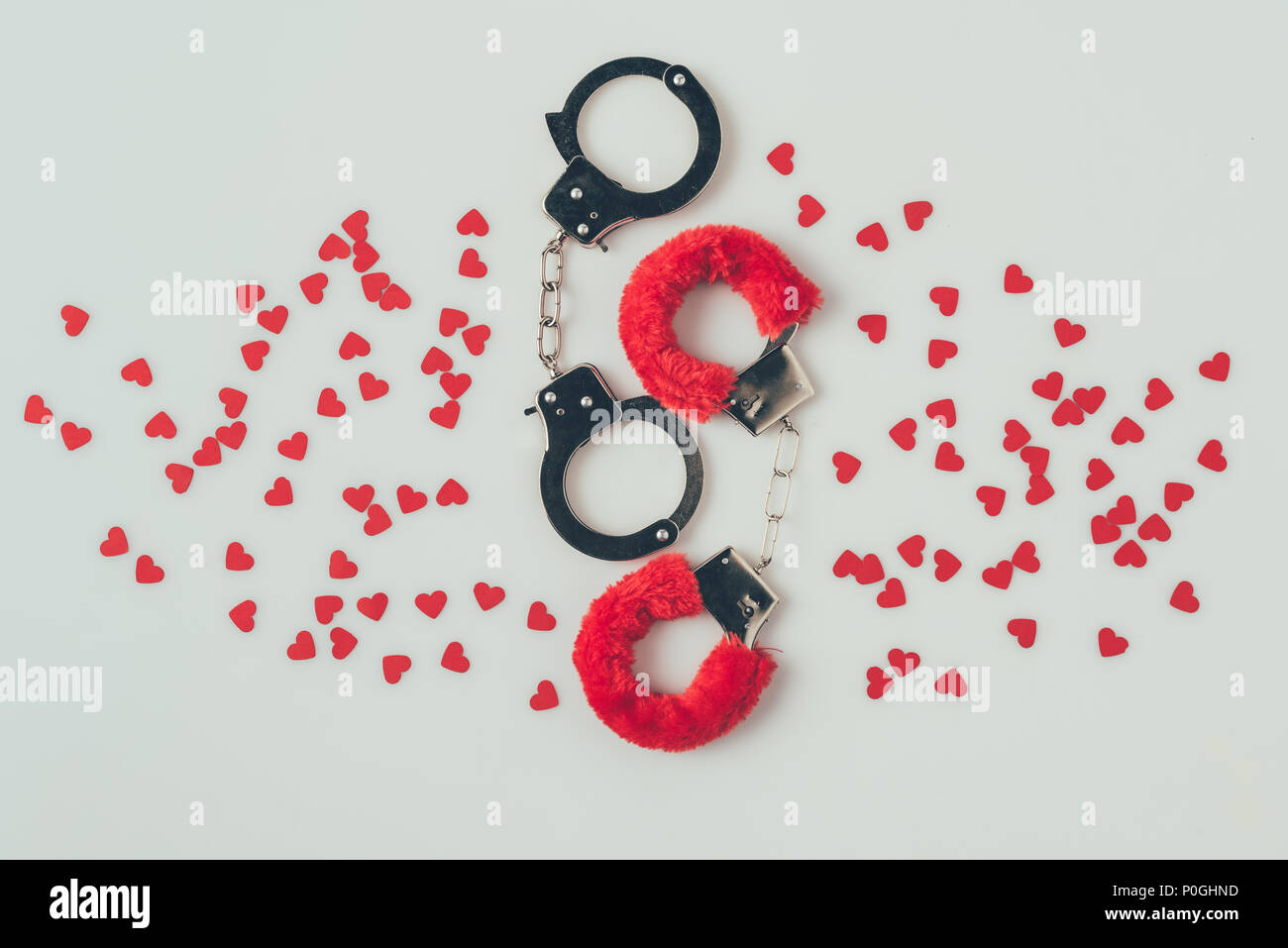 top view of black and red handcuffs with scattered paper hearts ...