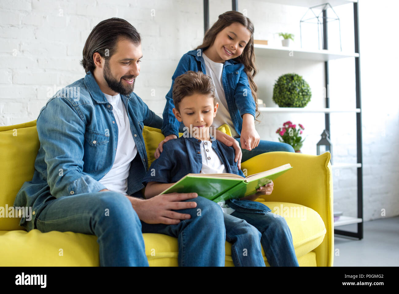 smiling father with two kids reading book together while sitting on ...