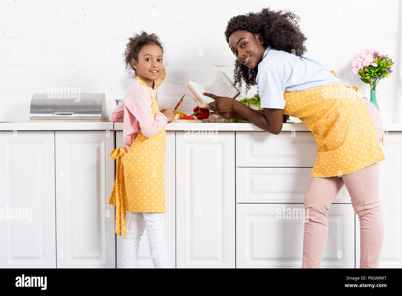 african american mother and daughter cooking with cookbook on kitchen ...