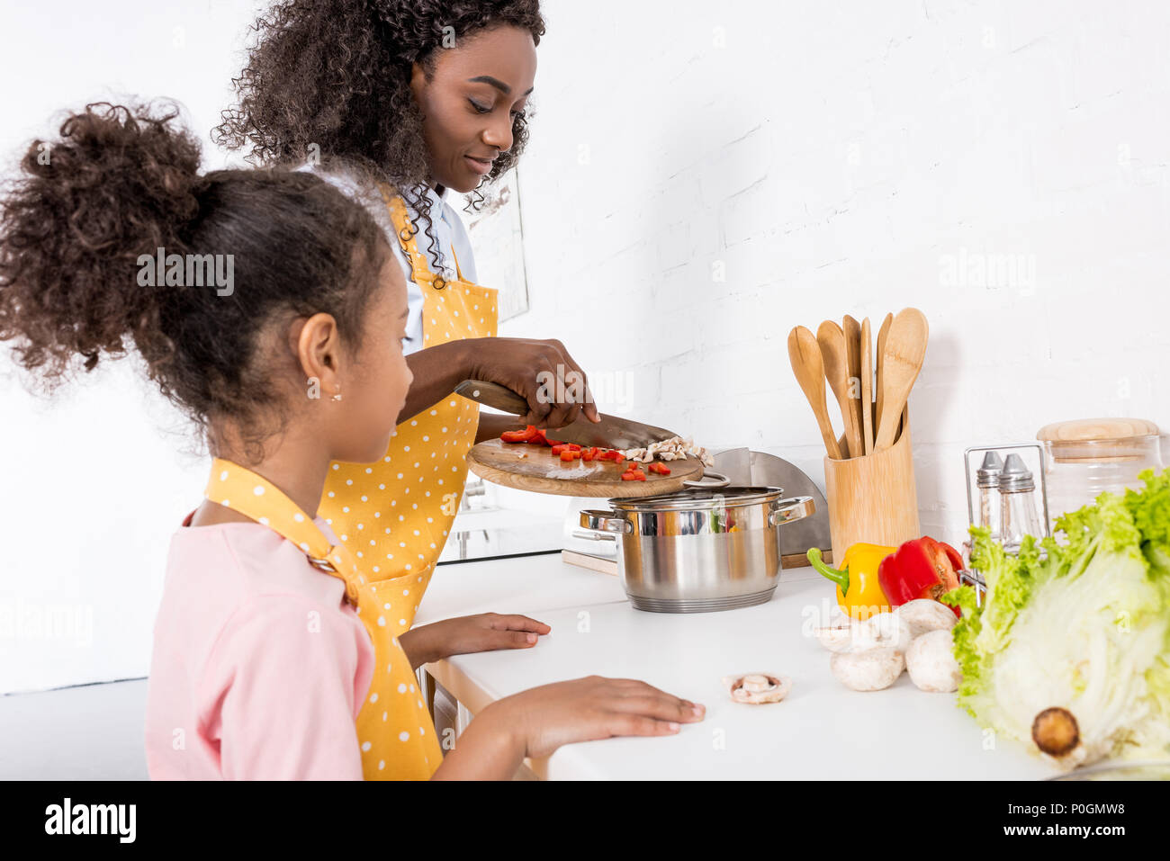 african american mother and daughter putting ingredientes in saucepan ...