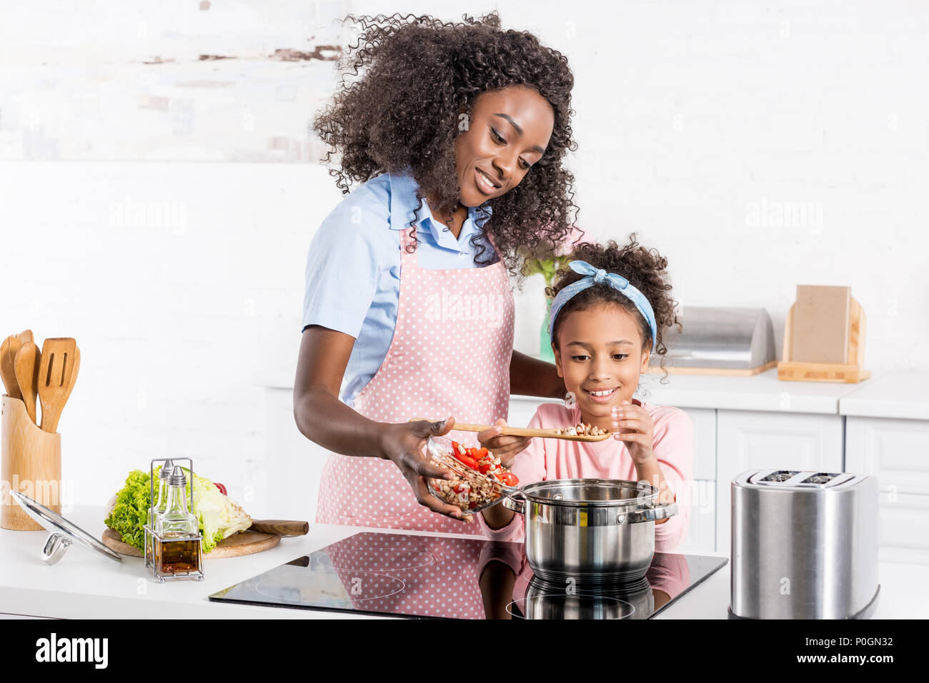 african american mom and daughter cooking on electric stove together Stock Photo Alamy