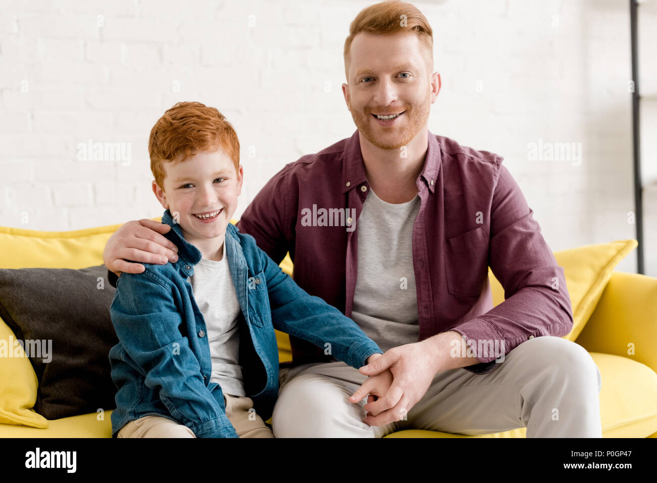 happy redhead father and son smiling at camera while sitting together ...