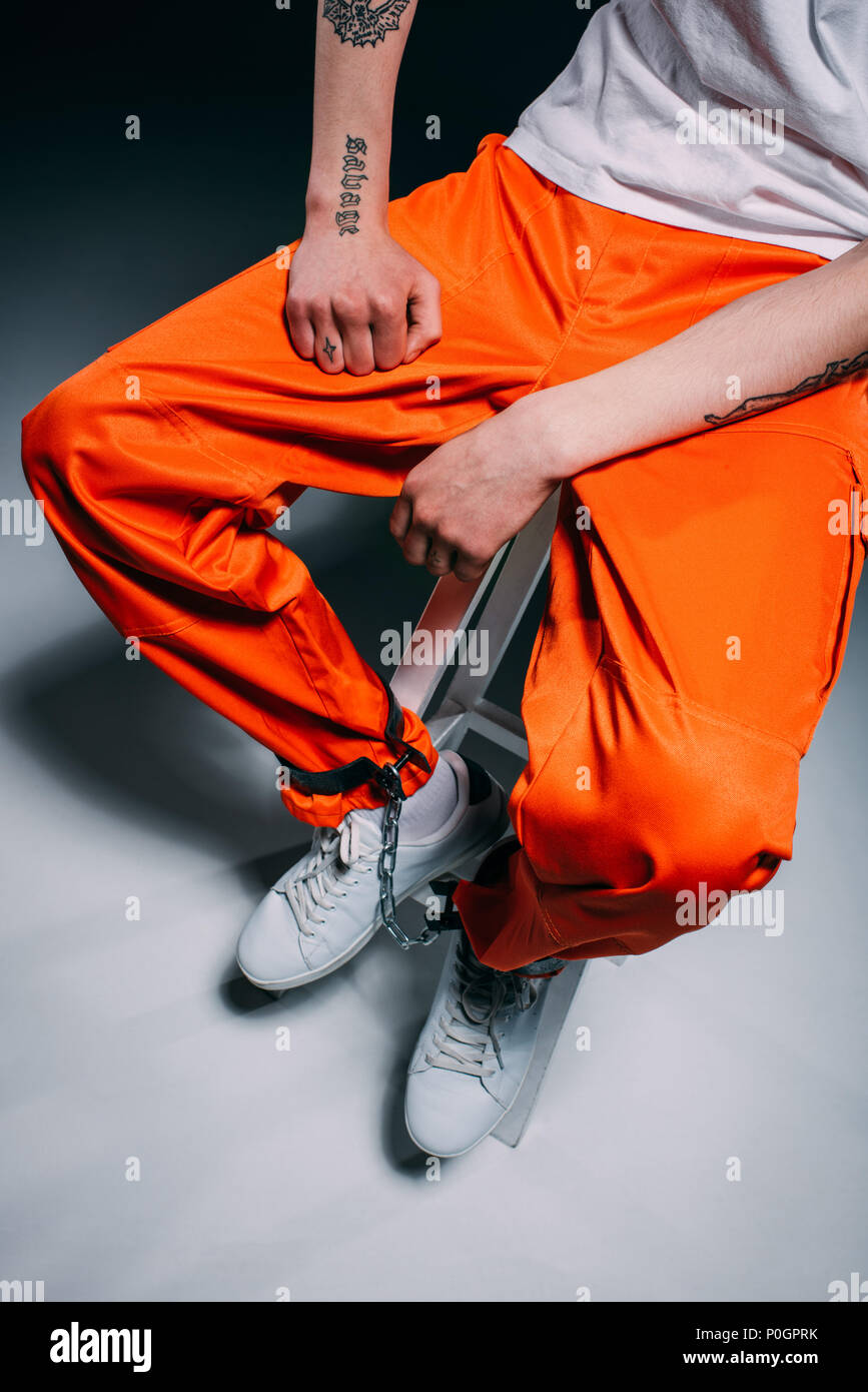 Top view of man in prison uniform with cuffs on legs sitting on stool ...