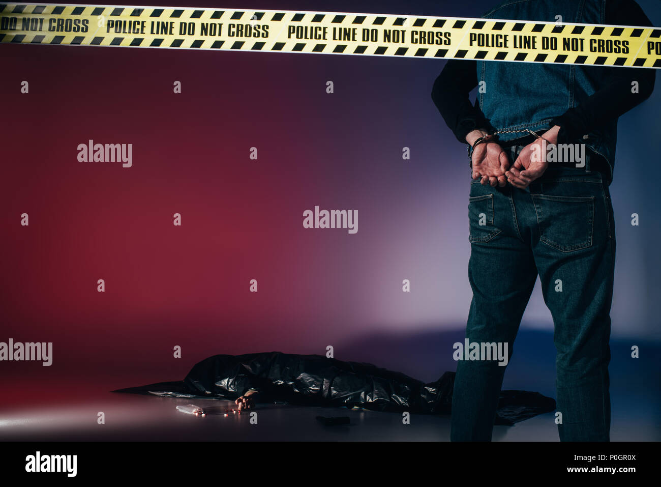 Rear view of murderer in cuffs behind police line on dark background ...