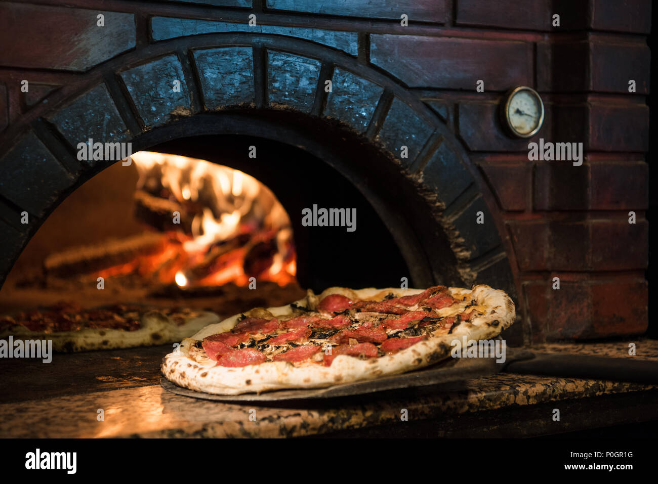 close up view of cooking process of raw pizza on wooden stove in brick ...