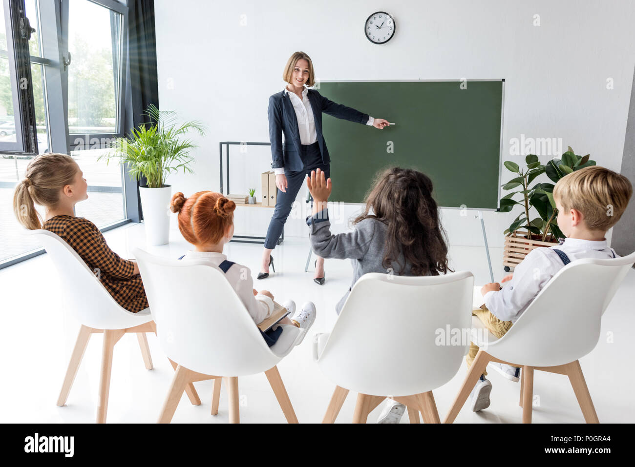 young female teacher pointing at chalkboard while explaining lesson to ...