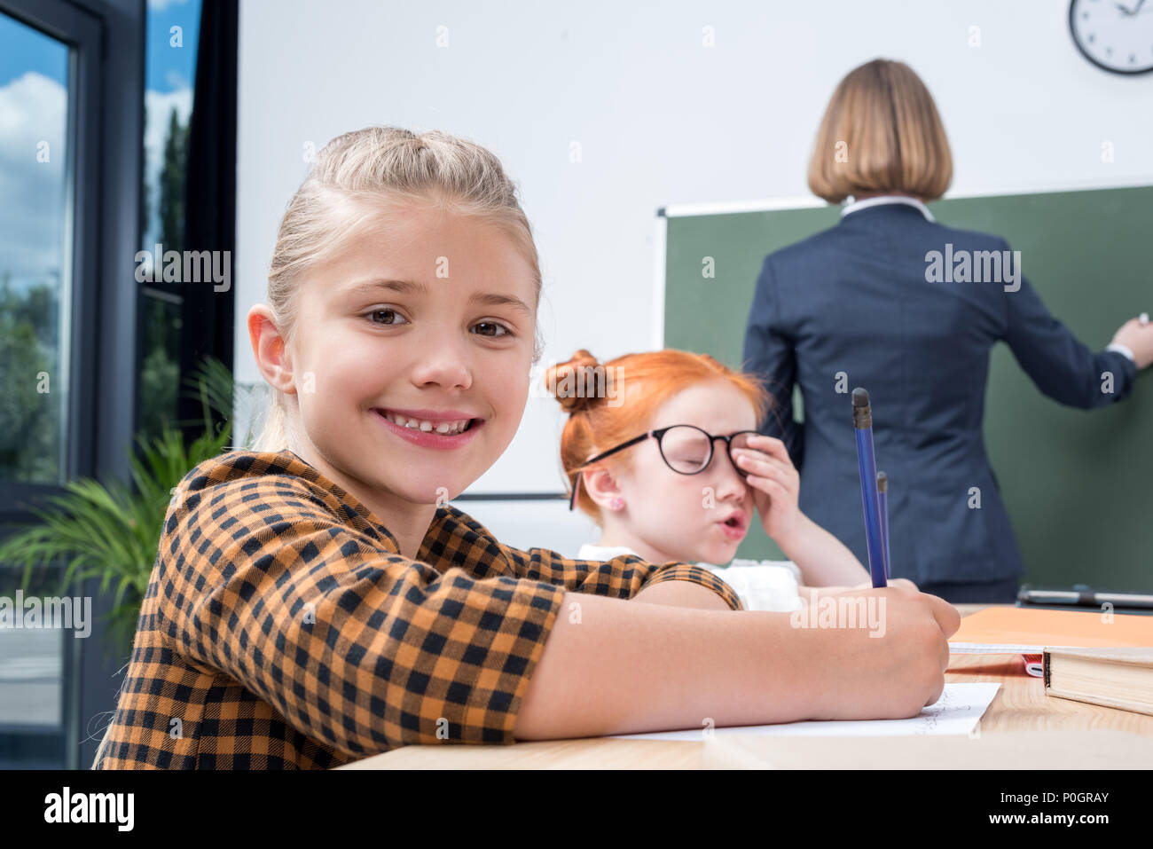 back view of teacher writing on chalkboard while students studying in ...