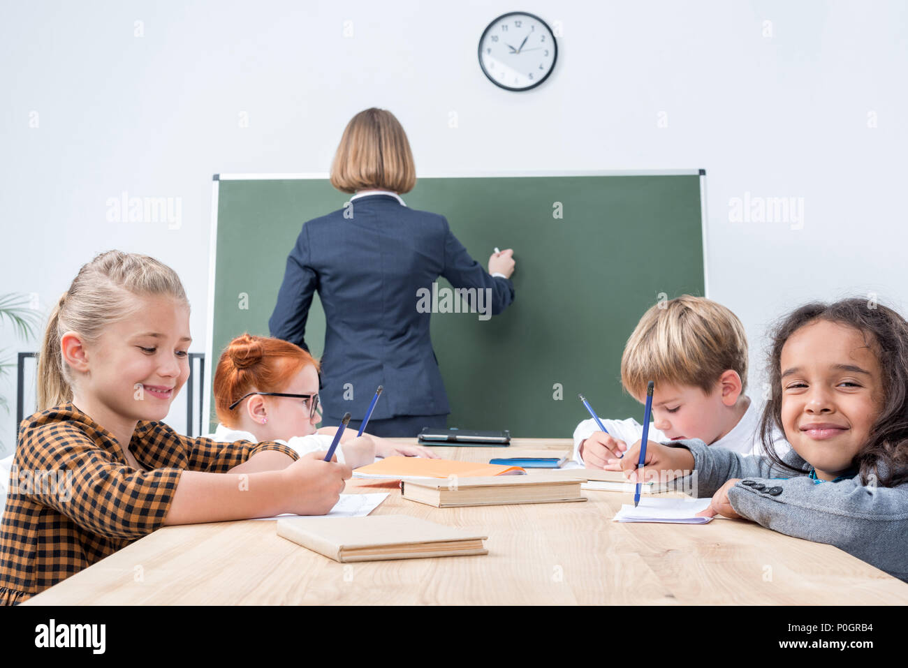 back view of teacher writing on chalkboard while students studying in ...