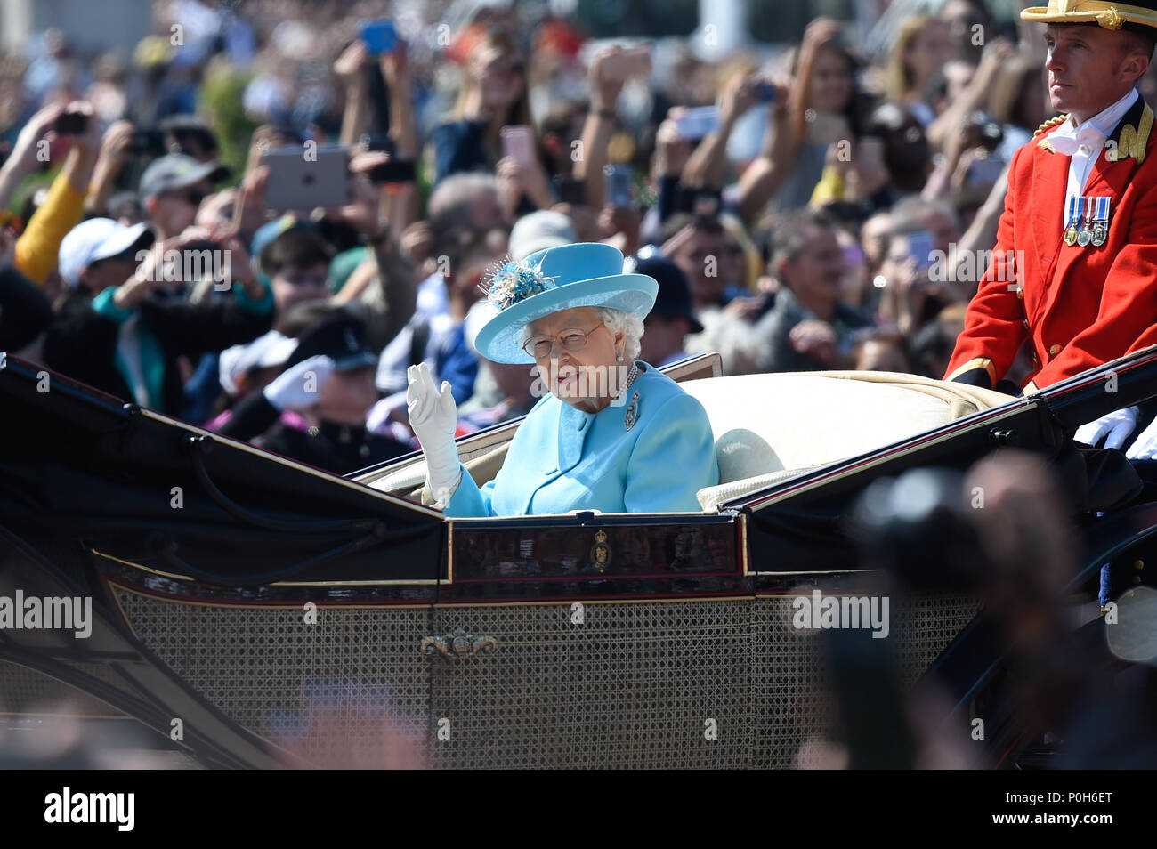 Queen Elizabeth II, waves to the crowds as she in rides in a carriage ...