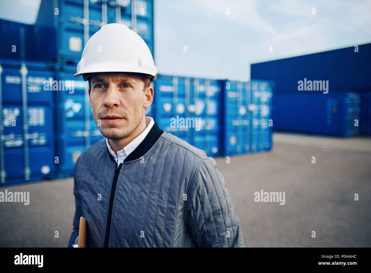 Port manager wearing a hardhat standing alone among freight containers ...
