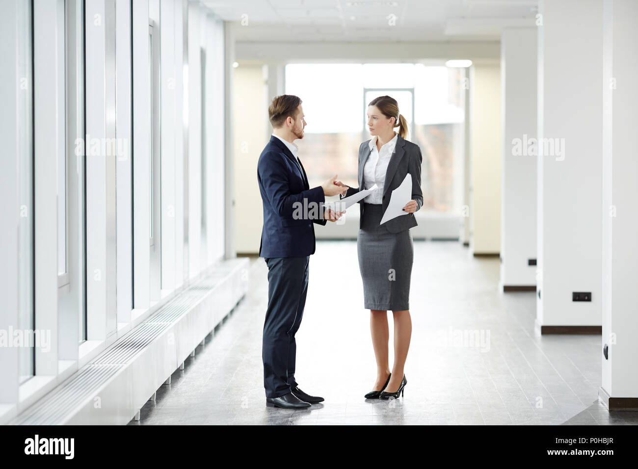 Two coworkers communicating in the modern corridor. They are discussing ...
