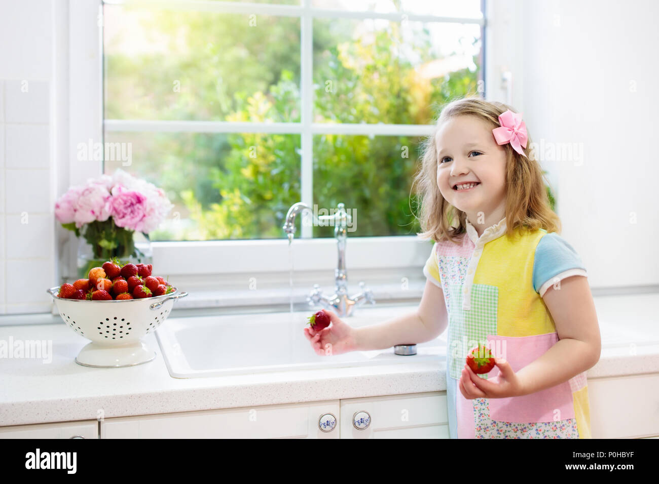 Cute little girl washing fruit in kitchen sink. Child eating strawberry ...