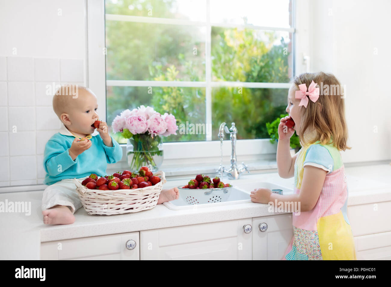 Little girl and baby boy washing fruit in kitchen sink. Children eat ...